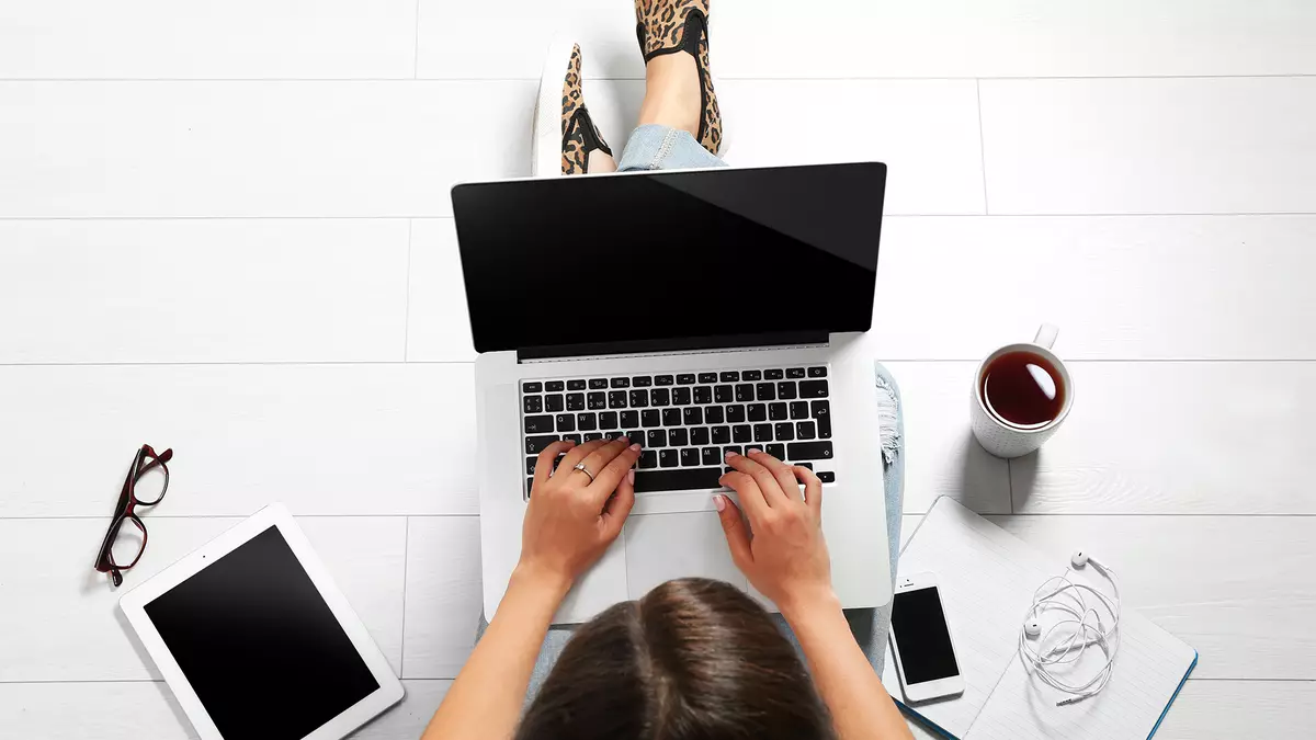 Una donna seduta sul pavimento e digitando su un MacBook.