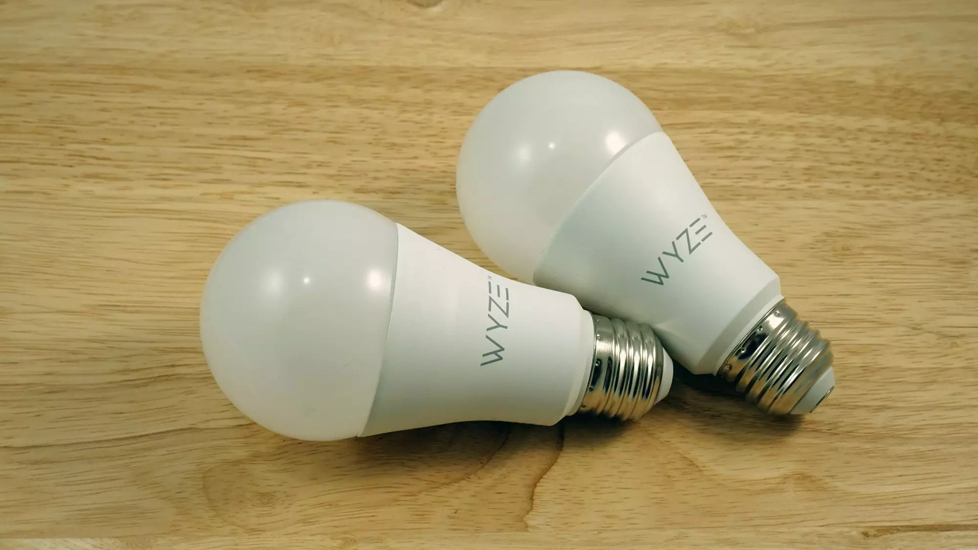 በእንጨት ጠረጴዛ ላይ ሁለት Wyze Smart Bulbs.