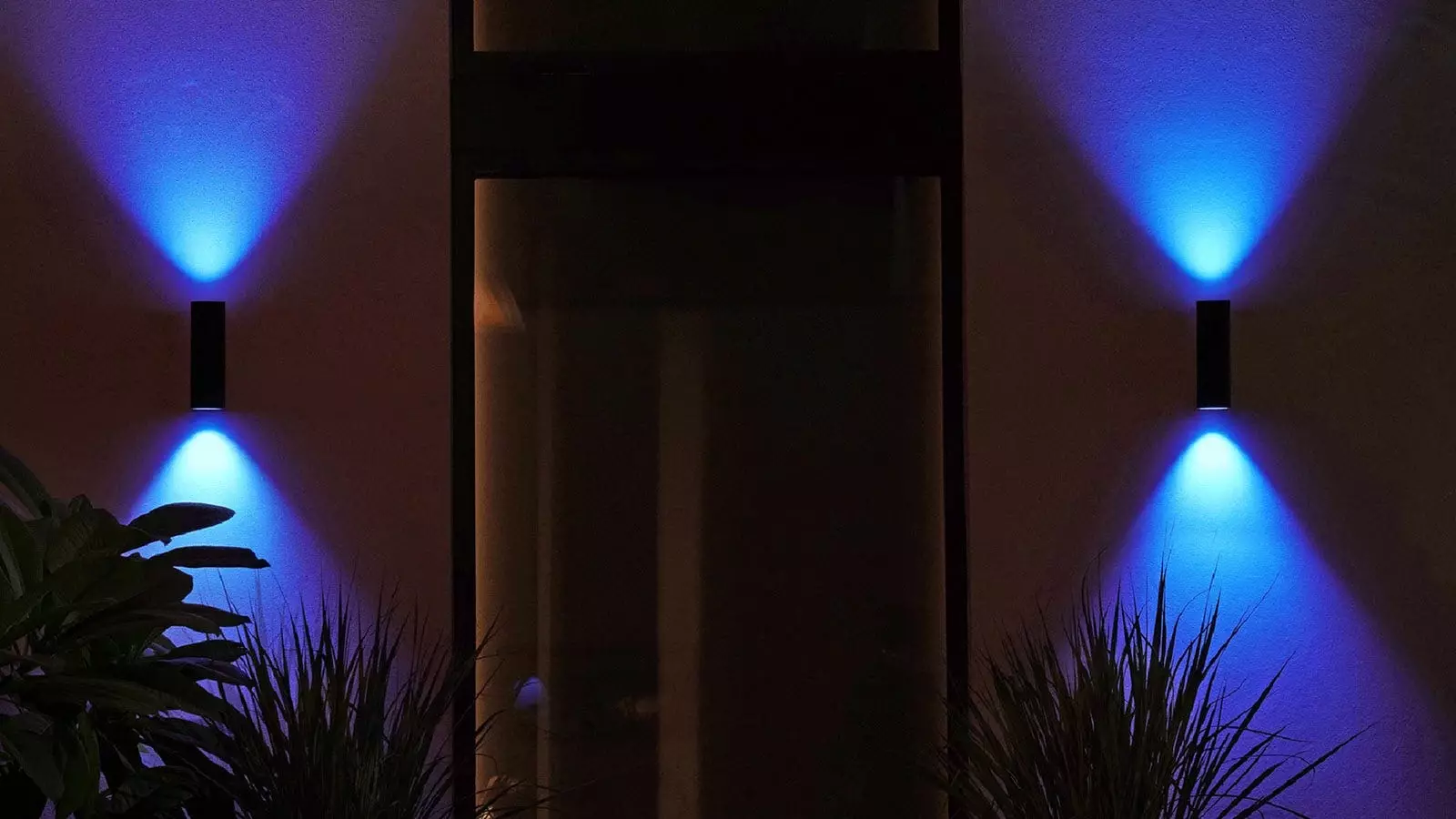 To vægmonterede lamper, der skinner blåt, lyser op og ned lodret.