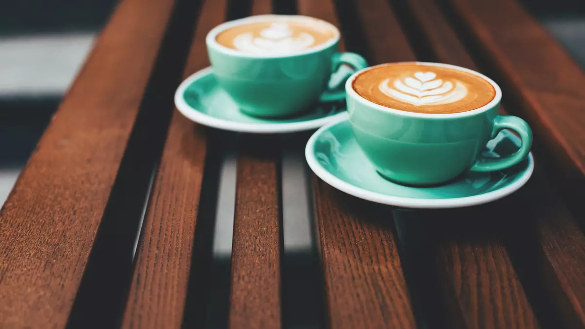 Rong cangkir cappuccino kanthi seni latte ing latar mburi kayu.