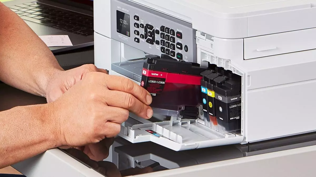 Moške roke vstavljajo tiskalniško kartušo v tiskalnik.