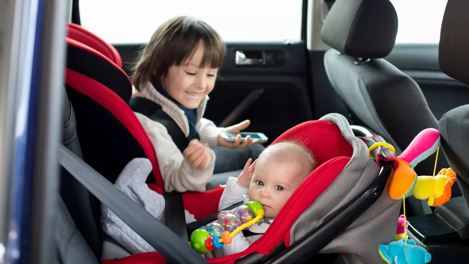 Mazs bērns un mazulis savos auto sēdekļos.