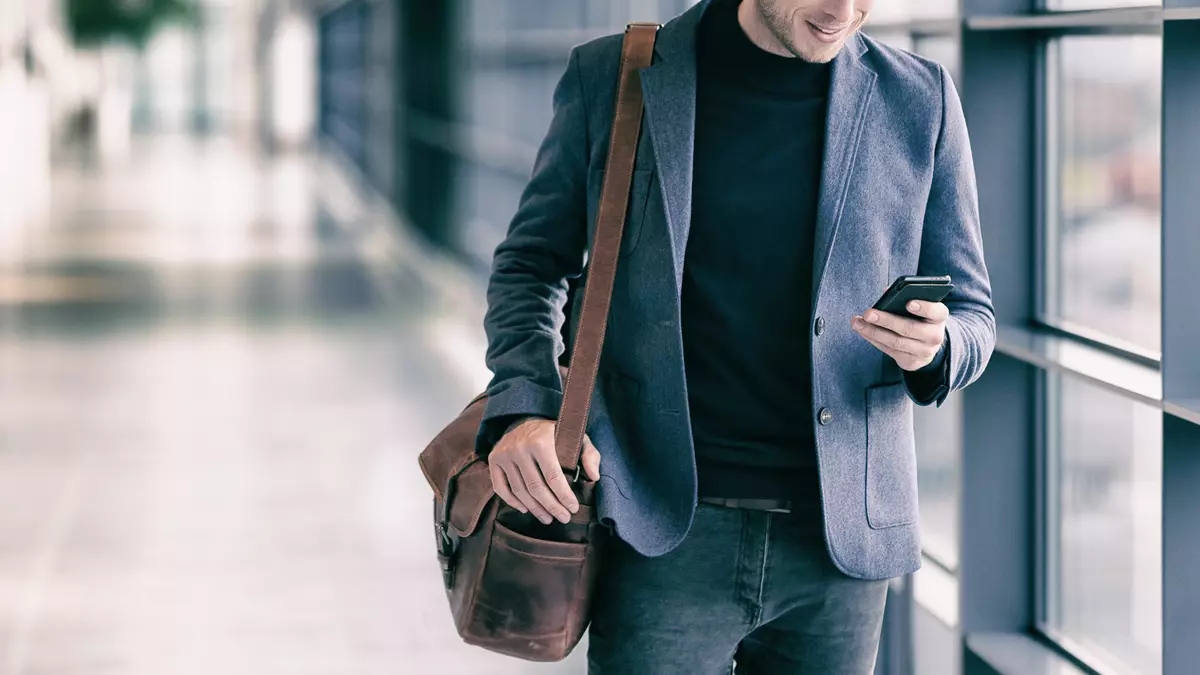 Un hombre mirando su teléfono y cargando una bolsa de mensajero en su hombro.