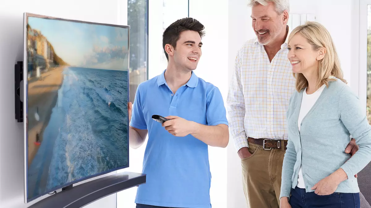 Mężczyzna pokazuje rodzicom swój schludny, zakrzywiony telewizor. Wydają się dumni.