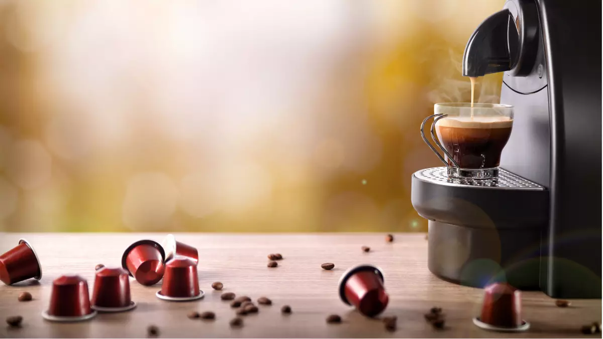 מכונת אספרסו ממלאת כוס עם כוסות K ריקות ופולי קפה מפוזרים סביבה.