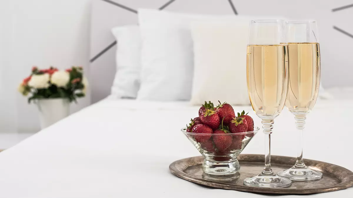 一杯香槟和一碗草莓放在昂贵的床垫上。