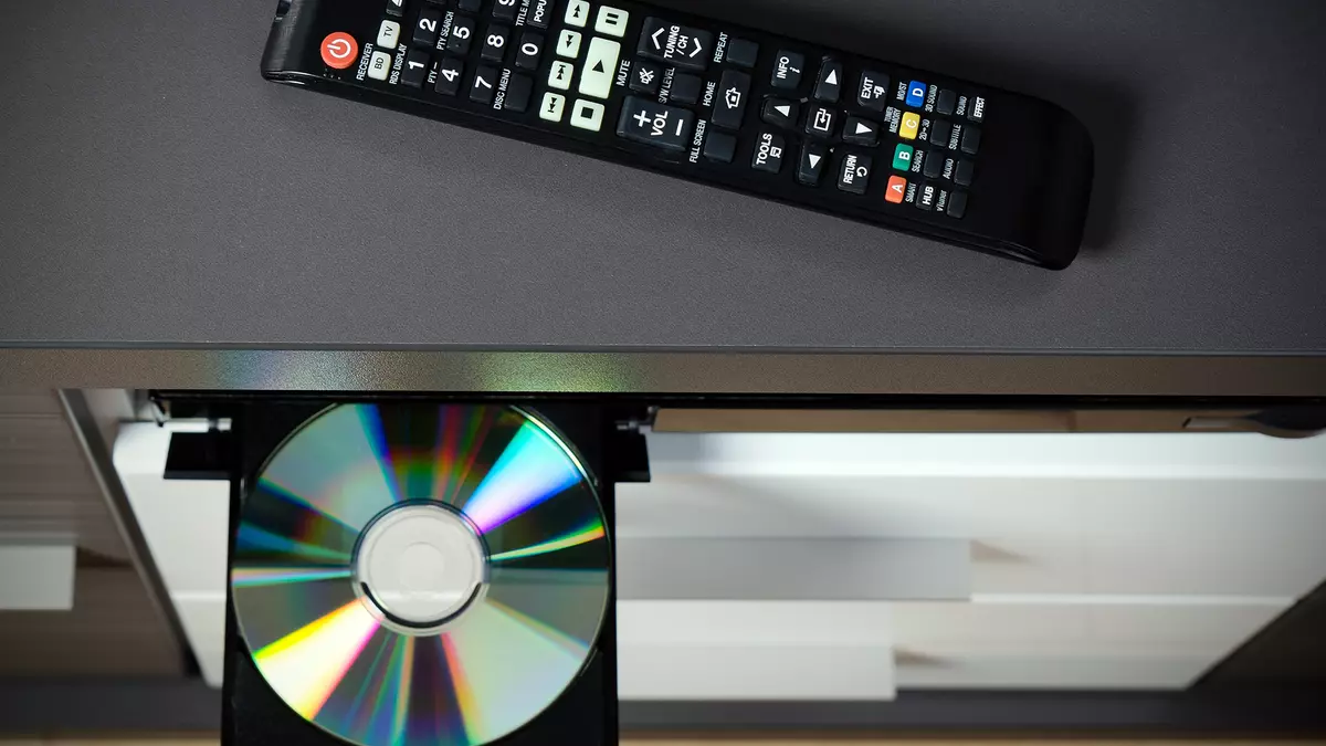 DVD terletak di atas dulang dalam pemain DVD, dan alat kawalan jauh pada rak di atas.