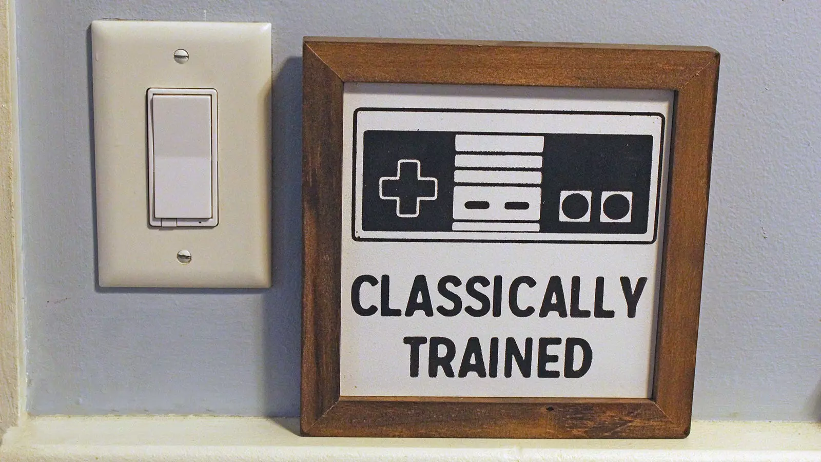 En smart switch med en paddelliknande vipp i en vägg bredvid en skylt som visar en NES-kontroller och orden