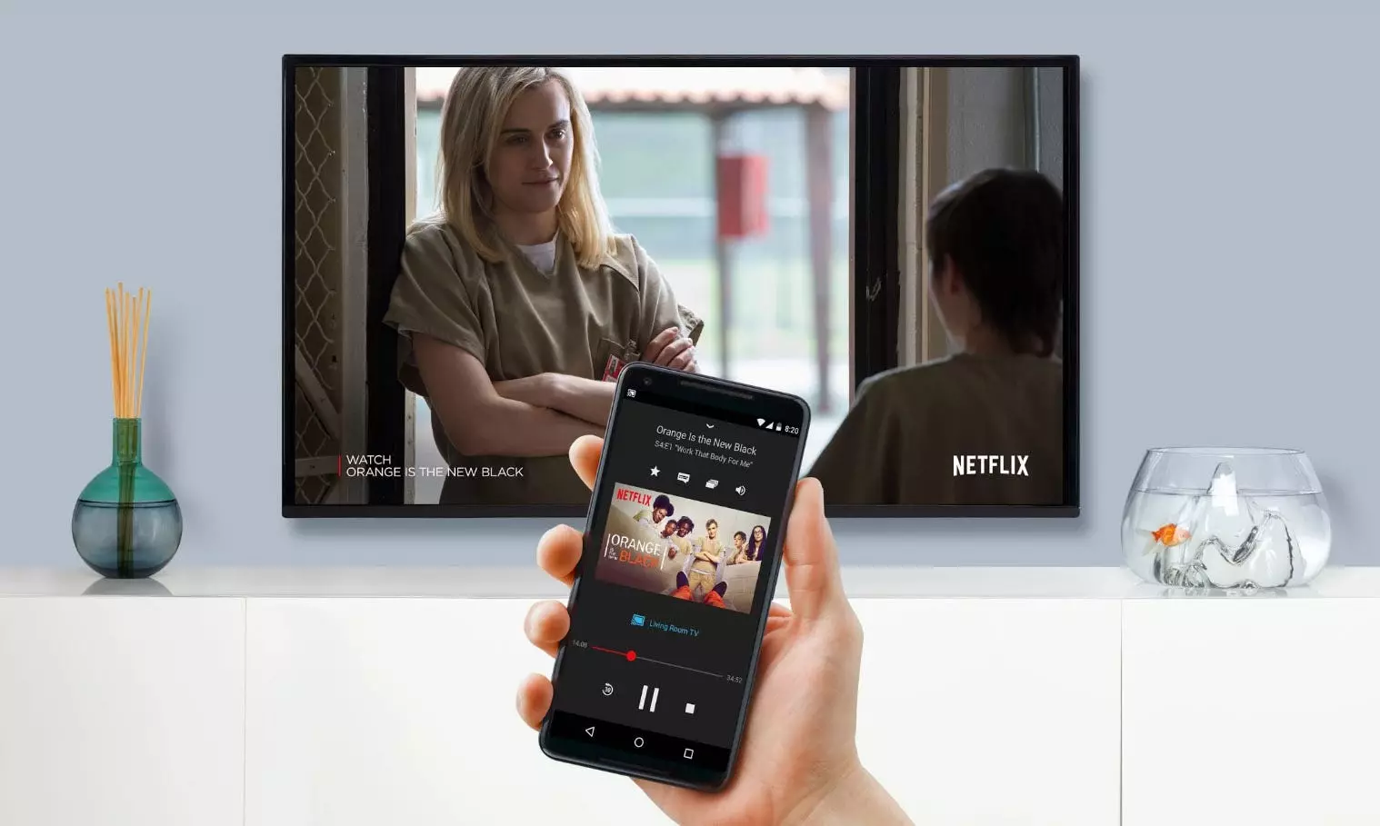 Die Hand eines Mannes, der ein Telefon hält, das Netflix auf einem Smart-TV mit großem Bildschirm betreibt.