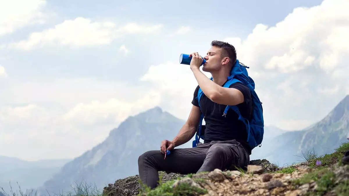Žmogus geria vandenį iš izoliuoto vandens butelio, žygiuodamas kalno viršūnėje