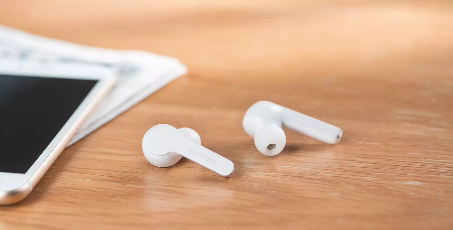Anker Soundcore Liberty Air trådlösa öronsnäckor i vitt, på ett träbord bredvid en iPhone