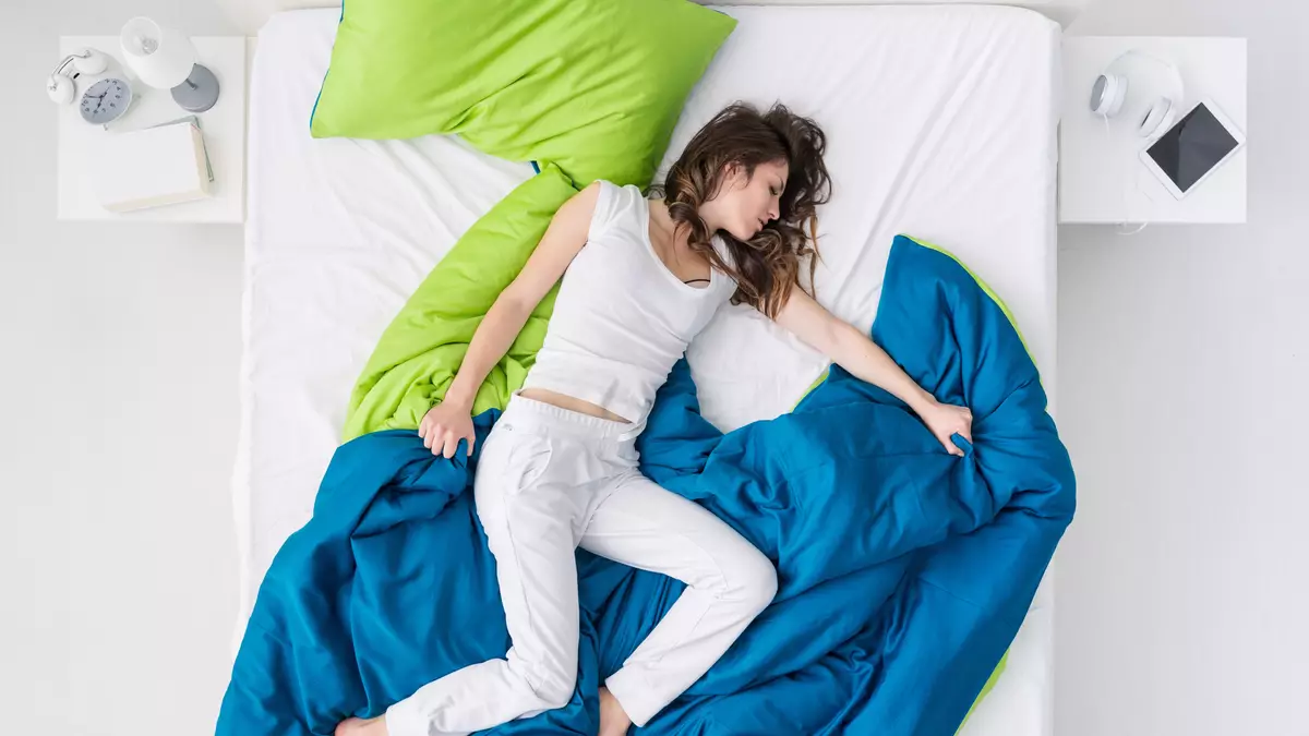 Wanita tidur di atas katil, cuba kekal sejuk pada waktu malam