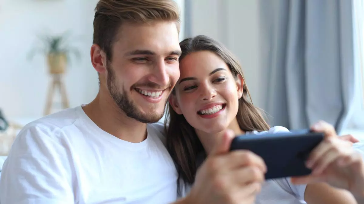 Šťastný usmievavý pár, ktorý sleduje hru kostí na mobilnom telefóne