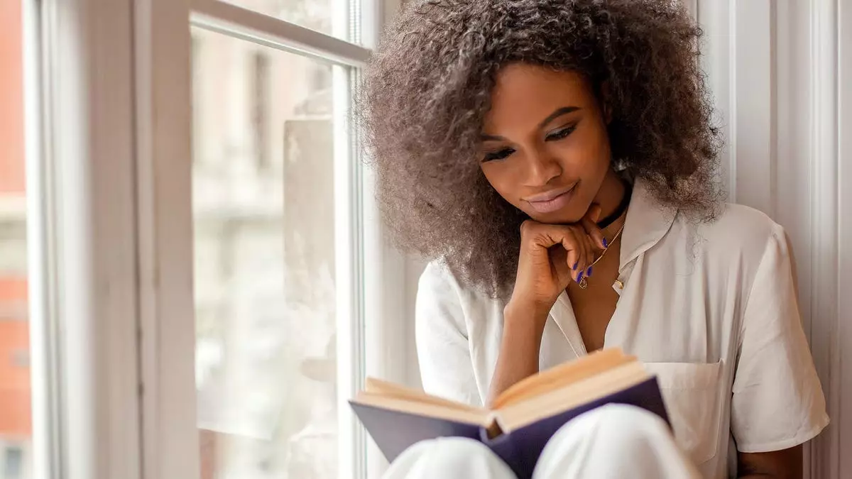 Gruaja duke lexuar një libër, e ulur në një dritareje