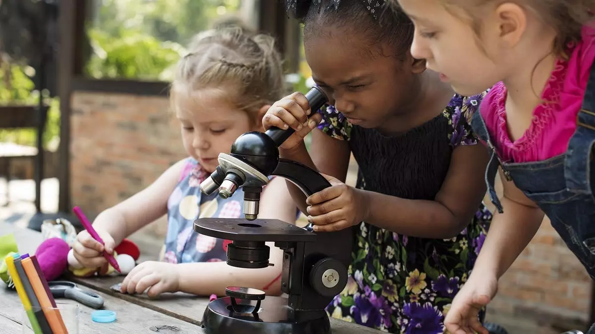 Os nenos pequenos usando o microscopio aprenden a clase de ciencias