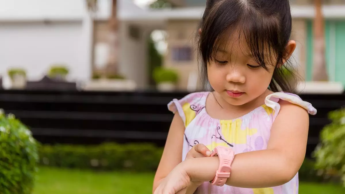 niña, afuera en un patio, mirando un reloj inteligente en su muñeca