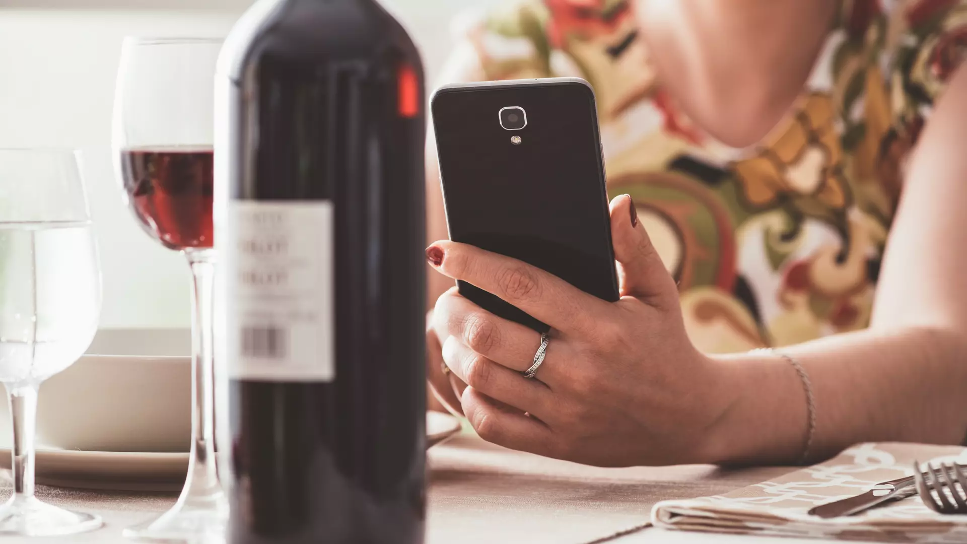 Muller almorzando no restaurante e usando unha aplicación de viño co seu teléfono intelixente, está escaneando a etiqueta da botella de viño