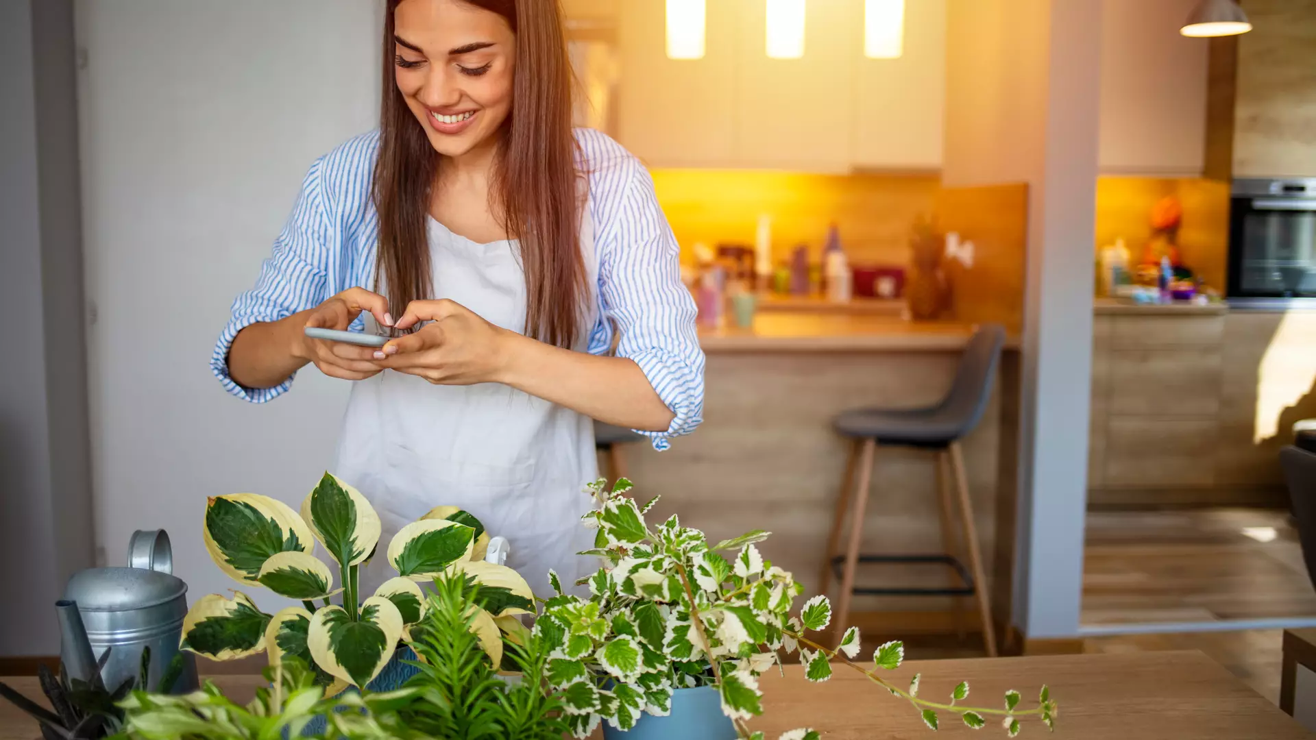 Срећна жена која слика зелене биљке и цвеће паметним телефоном. Жена слика зелене биљке. Жена брине о кућној биљци.