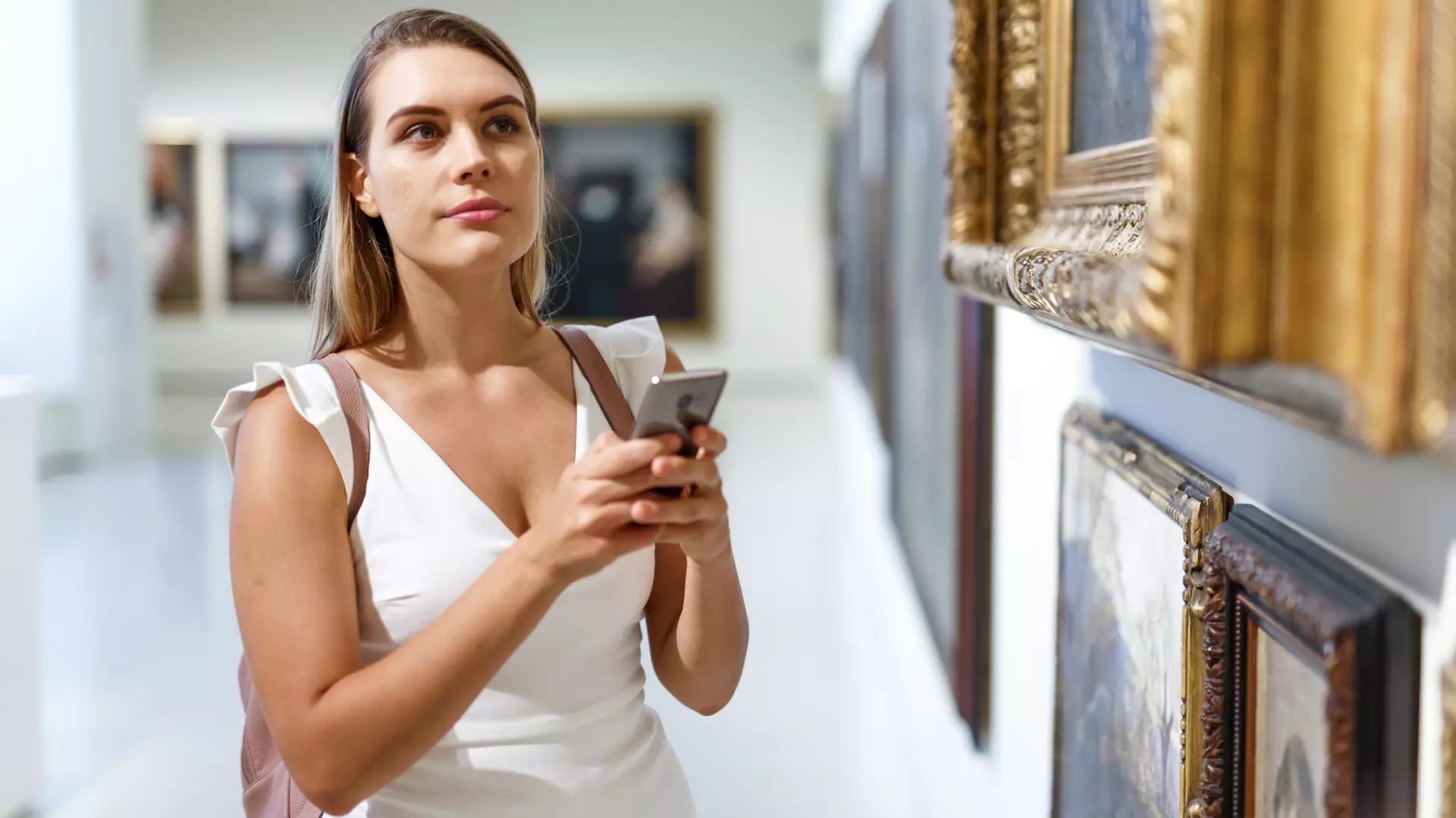 Intelektuali jauna moteris telefonu ieško informacijos apie tapybą muziejuje